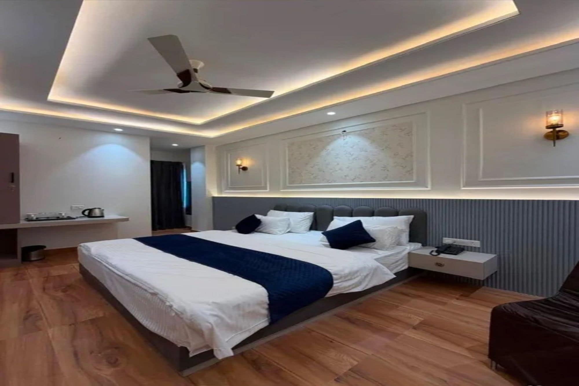 Quarto de hotel moderno com uma cama grande, mesas de cabeceira, escrivaninha e ventilador de teto.