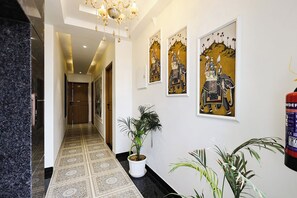 Corredor de hotel com piso estampado, planta em vaso e quadros nas paredes.