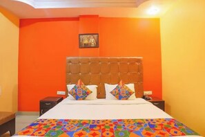 Quarto de hotel com cama grande, paredes laranja e um quadro emoldurado acima da cama.
