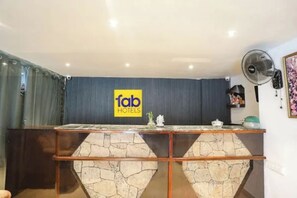 Bancada de recepção com placa 'fab hotels', um ventilador e uma planta decorativa.