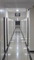 Um corredor comprido e estreito, com portas em ambos os lados, piso ladrilhado e câmera de segurança no teto.