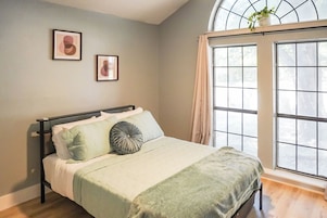 Quarto com uma cama, janela com cortinas e duas imagens emolduradas na parede.