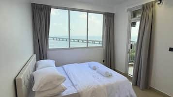 Quarto de hotel com cama, ventilador de teto, janela com cortinas e vista para o mar.