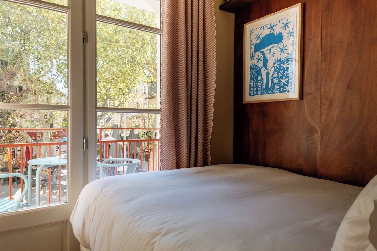 Quarto de hotel com uma cama grande, janela com cortinas e vista para o exterior.