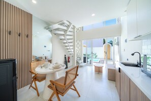 Uma cozinha moderna com ilha central, cadeiras de madeira e escada em espiral que leva a um andar superior.