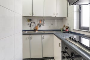 Cozinha com armários brancos, pia de aço inoxidável e cafeteira no balcão.