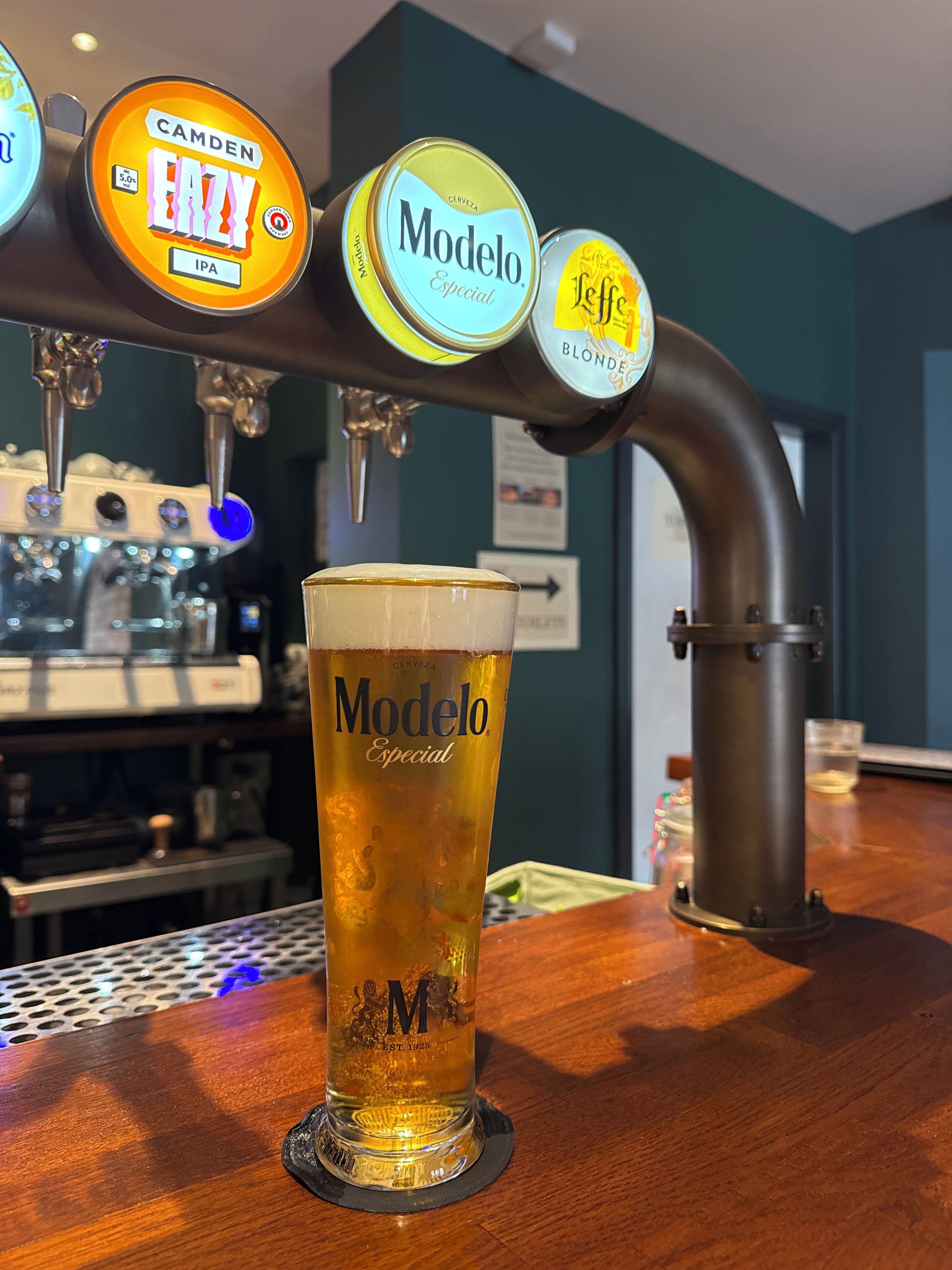 Uma torneira com cerveja Modelo e um copo de cerveja em um balcão de bar.