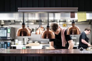 Cozinha com luminárias pendentes de cobre, bancada de madeira e uma pessoa trabalhando no balcão.