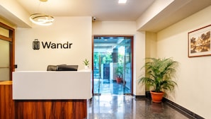 Balcão de recepção com uma placa que diz 'Wandr' e uma planta em vaso à direita.