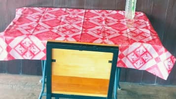 Uma pequena mesa com toalha xadrez vermelha e branca, uma cadeira com encosto de madeira e um vaso de planta em garrafa transparente.