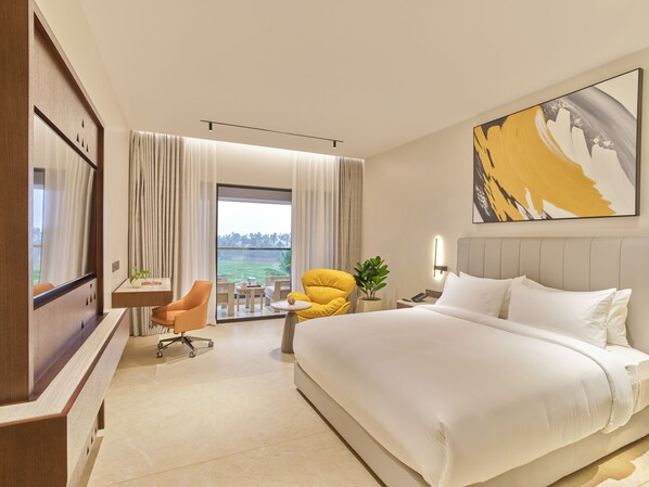 Quarto de hotel com uma cama grande, uma escrivaninha, uma cadeira, uma varanda com vista e um quadro na parede.