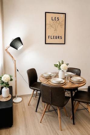 Uma sala de jantar com mesa redonda posta para quatro pessoas, rodeada por cadeiras de couro, um abajur e uma placa emoldurada acima.