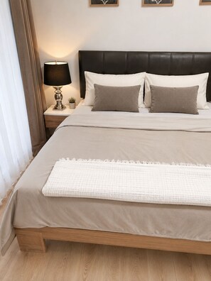 Cama bem arrumada com colcha branca, cabeceira escura e abajur.