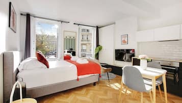 Quarto de hotel moderno com cama, área de jantar e cozinha.