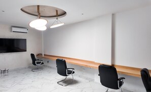 Uma sala de conferências com piso de mármore, cadeiras pretas, uma estante de madeira e uma televisão de tela plana.