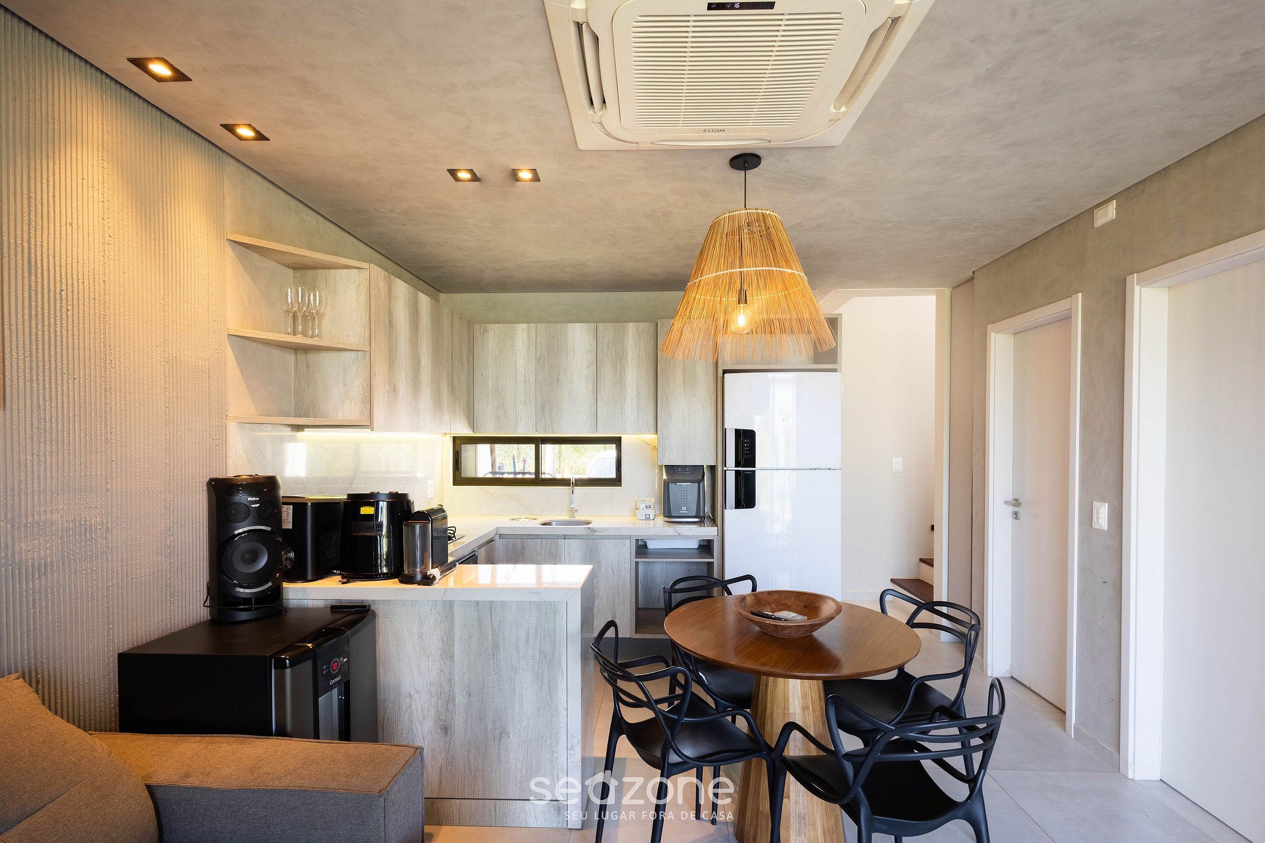 Cozinha moderna com ilha central, eletrodomésticos embutidos e área de refeições com mesa redonda e cadeiras.