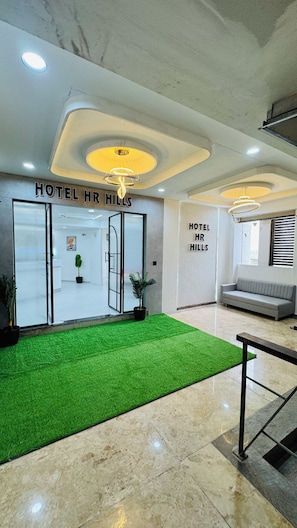Um balcão de recepção de hotel com carpete verde, luminárias modernas e um sofá.