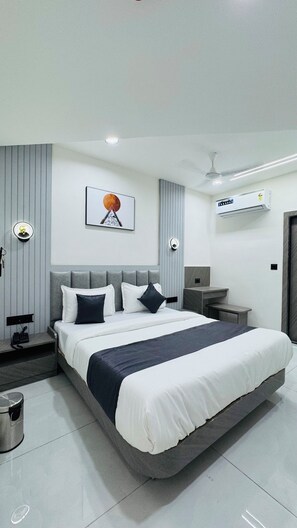 Quarto de hotel moderno com uma cama grande, mesas de cabeceira, ar condicionado fixado na parede e ventoinha de teto.