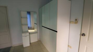 Quarto com armário branco, pequena escrivaninha e espelho.
