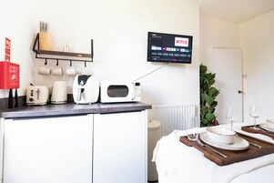 Cozinha compacta equipada com micro-ondas, torradeira e cafeteira, manta anti-incêndio e TV exibindo Netflix.
