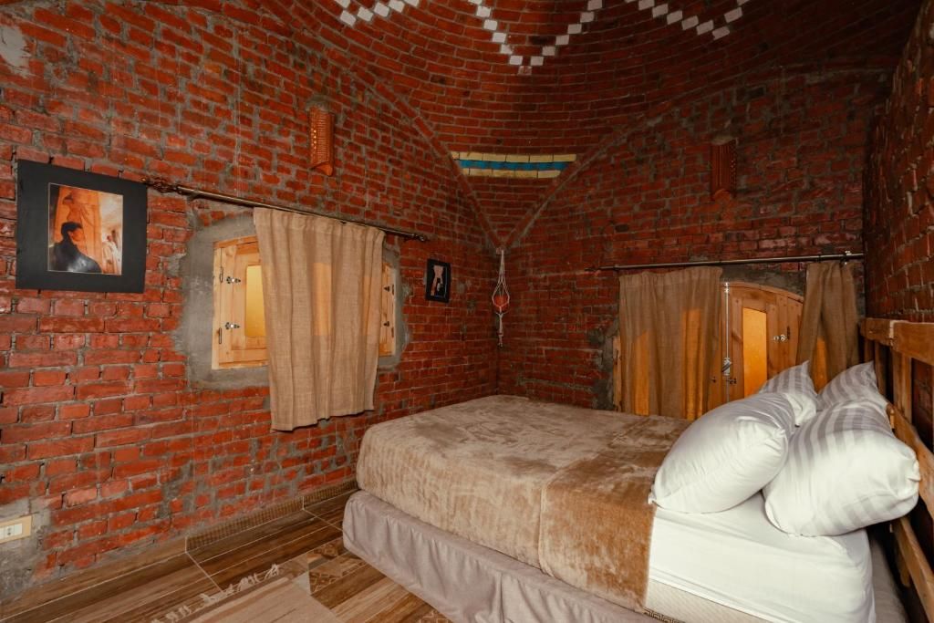 Quarto com parede de tijolos, cama com travesseiros, porta de madeira e um quadro na parede.