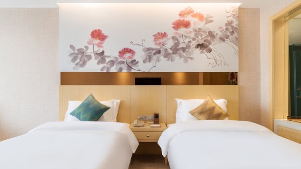 Quarto de hotel com duas camas, uma mesinha de cabeceira e televisão presa na parede.