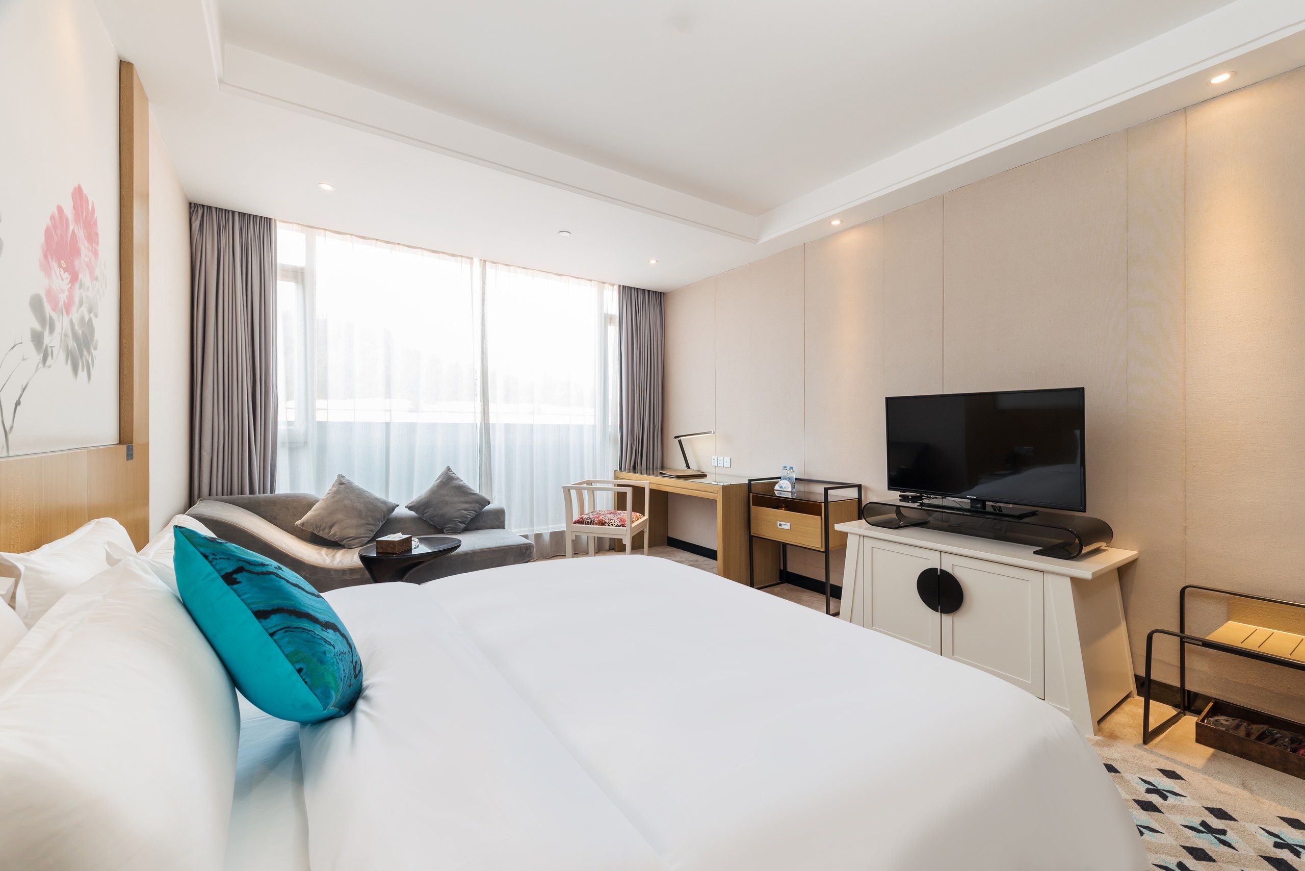 Quarto de hotel com cama grande, escrivaninha com televisão de tela plana, cadeira e janela com cortinas.
