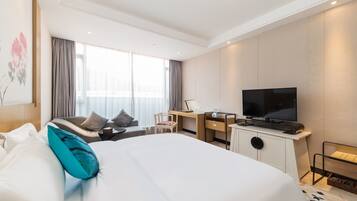 Quarto de hotel com cama grande, escrivaninha com televisão de tela plana, cadeira e janela com cortinas.