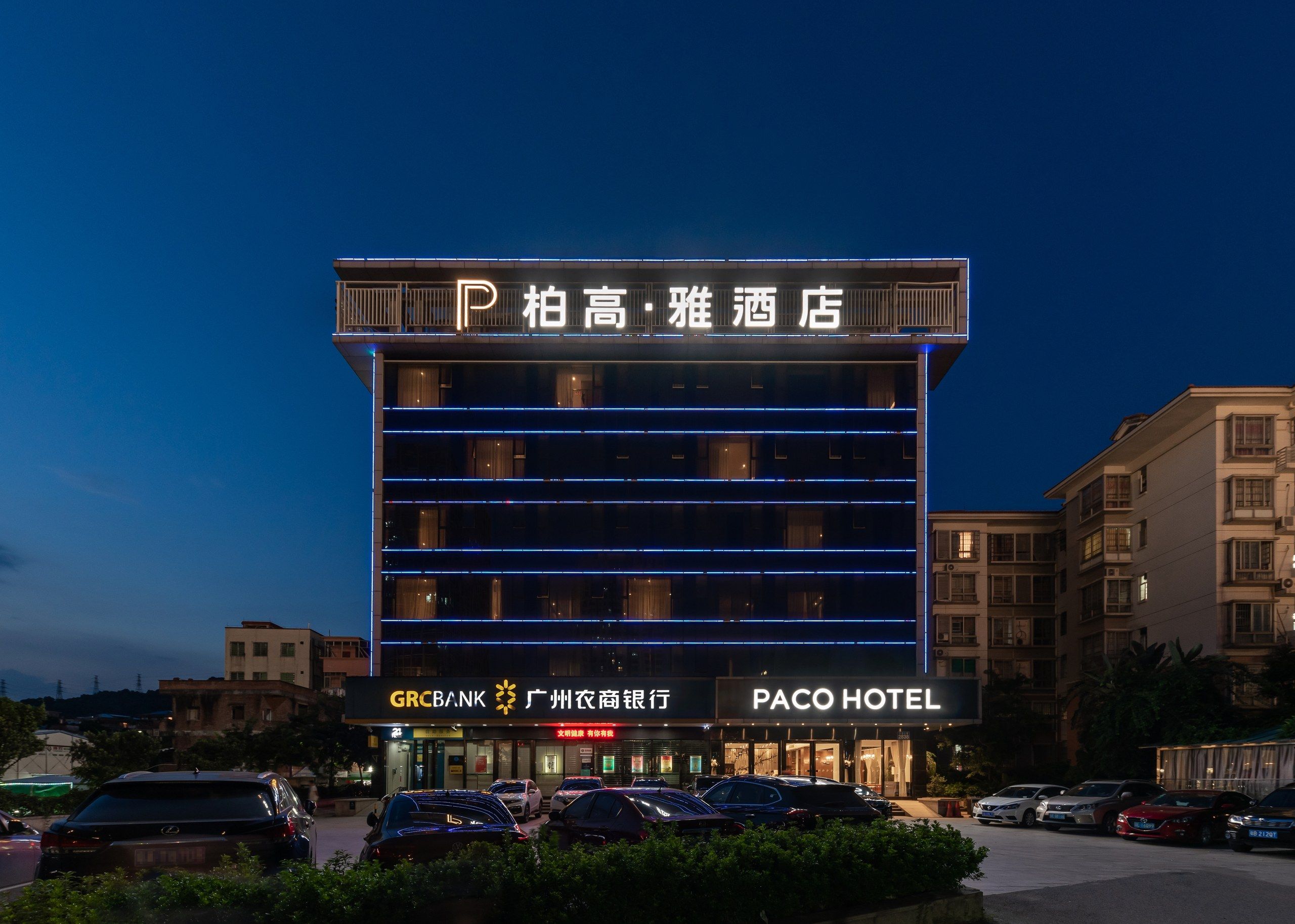 Um hotel com vários andares e fachada moderna, com letreiros iluminados para um banco e um hotel.