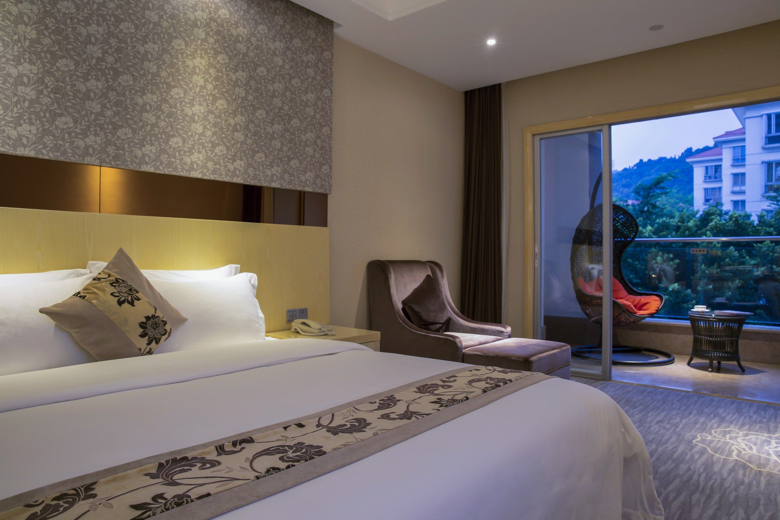 Quarto de hotel com uma cama grande, uma cadeira, um telefone e vista para um prédio por uma porta de vidro.