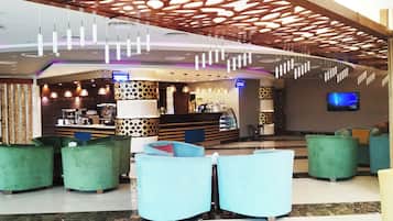 Um lobby moderno com balcão de recepção, área de estar e uma tela de TV.