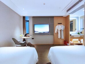 Quarto de hotel com duas camas, televisão, escrivaninha com cadeira e porta-toalhas.