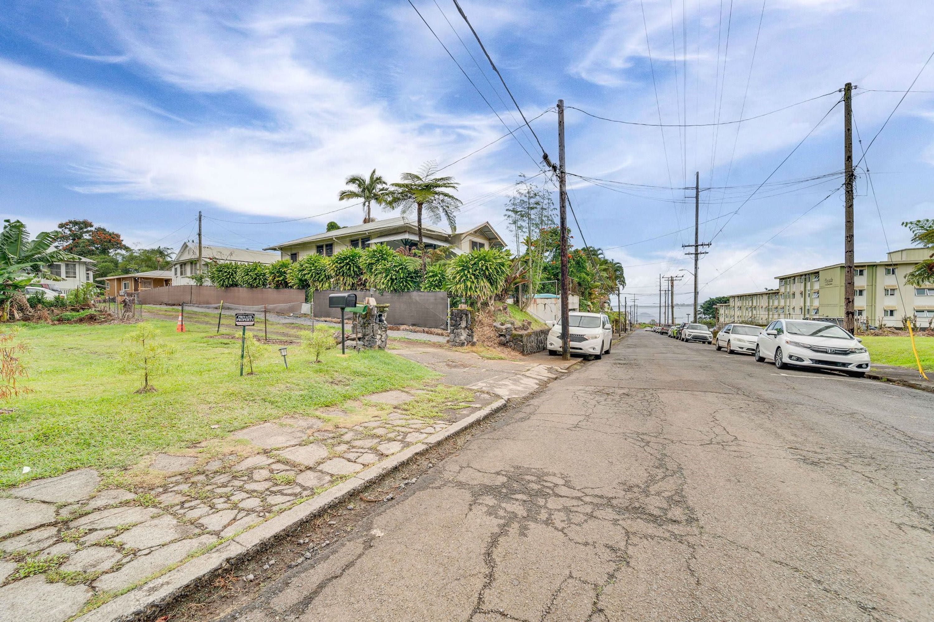Rua residencial com casas, carros estacionados e céu claro.
