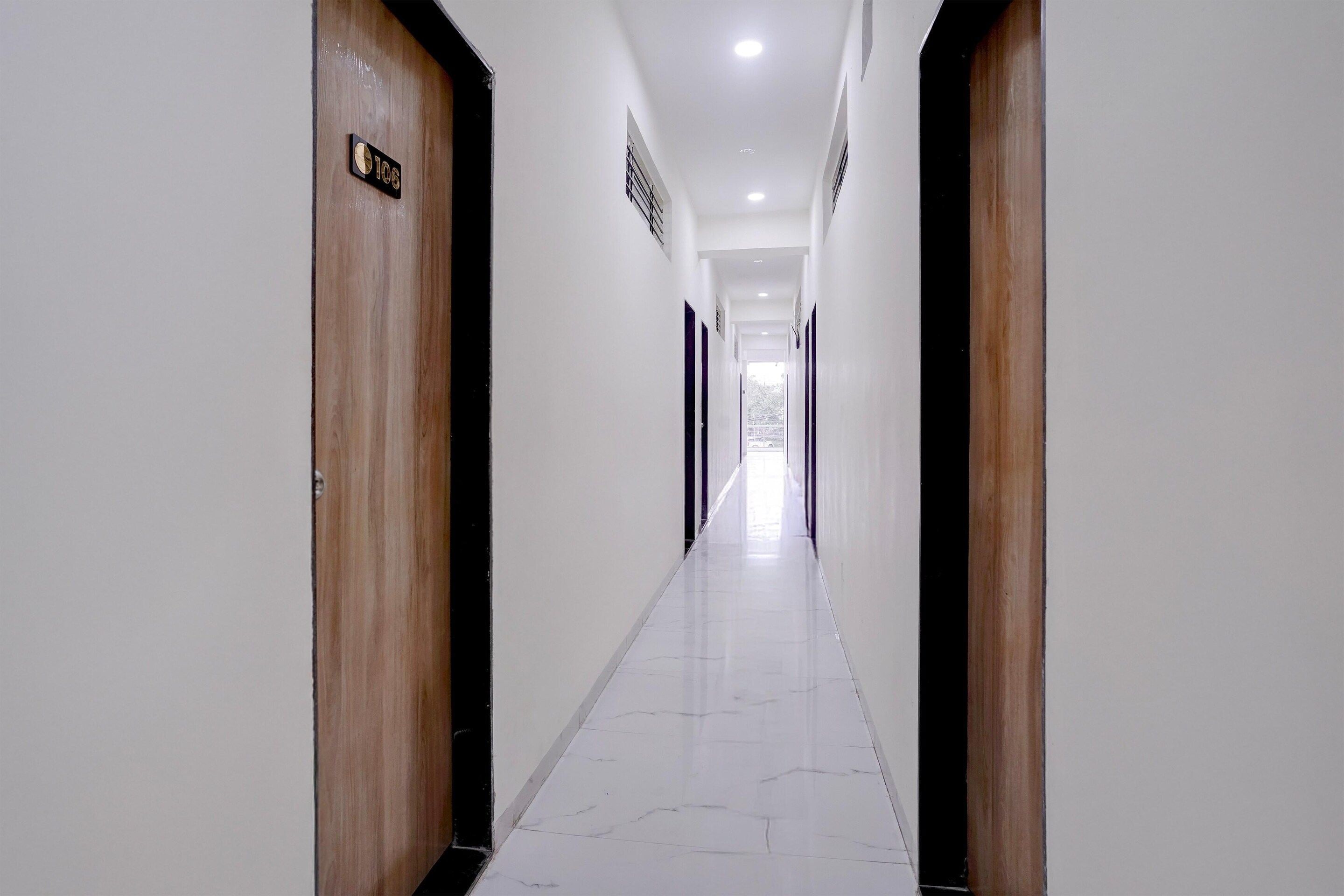 Um corredor comprido e estreito com portas de madeira em ambos os lados e piso de azulejos.
