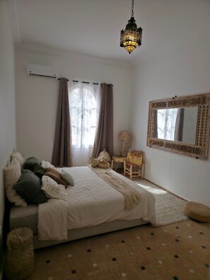 Quarto com cama, espelho, luminária pendente e janela com cortinas.