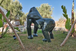 Escultura de animal em um jardim, com grama, árvores e um edifício ao fundo.