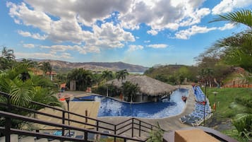 Área de piscina em resort com estrutura de palha, cadeiras de sol e vista para a paisagem ao redor.