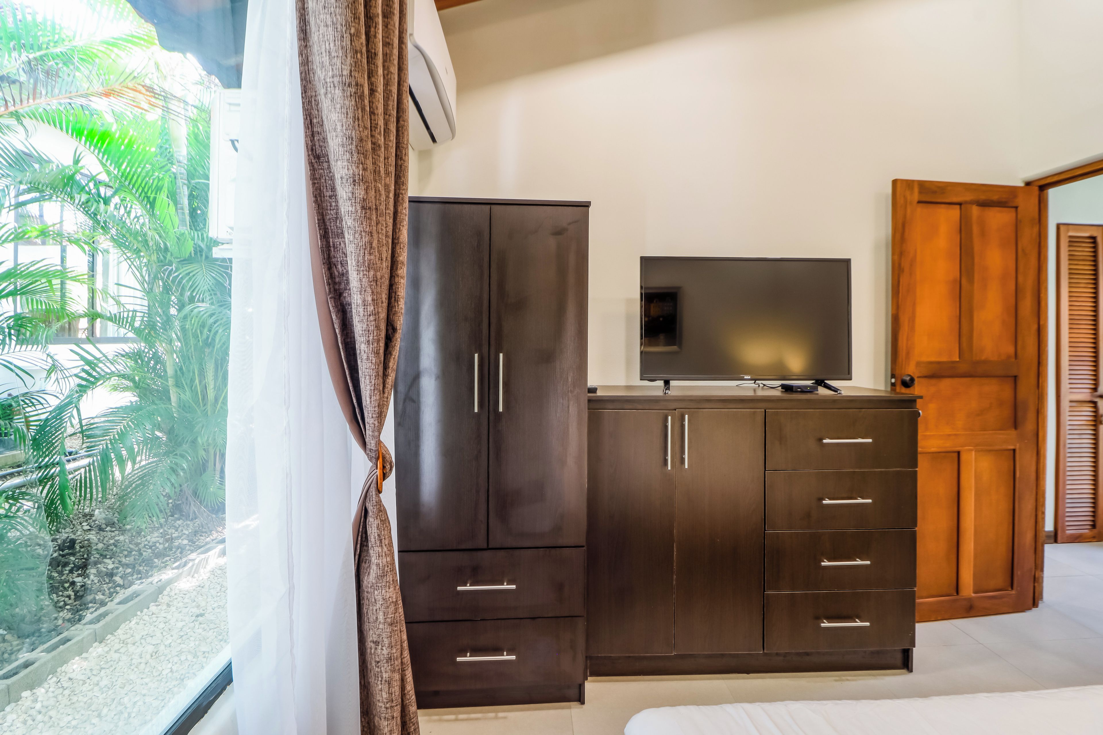 Quarto com guarda-roupa de madeira escura, uma TV de tela plana em cima e uma porta de madeira.