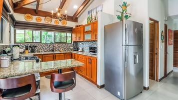Cozinha moderna com bancadas de granito, armários de madeira e geladeira de aço inoxidável.