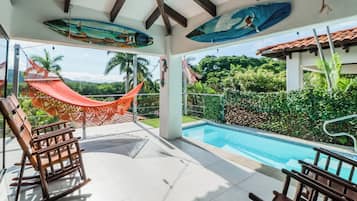 Área de piscina com rede, cadeiras e vista para o verde ao redor.
