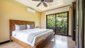 Quarto com cama de madeira, ventoinha no teto e vista para um jardim através de uma porta de correr.