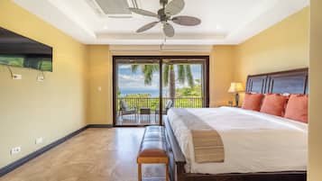 Quarto de hotel com cama, um banco, ventilador de teto, TV fixada na parede e vista para o exterior por uma porta de correr.