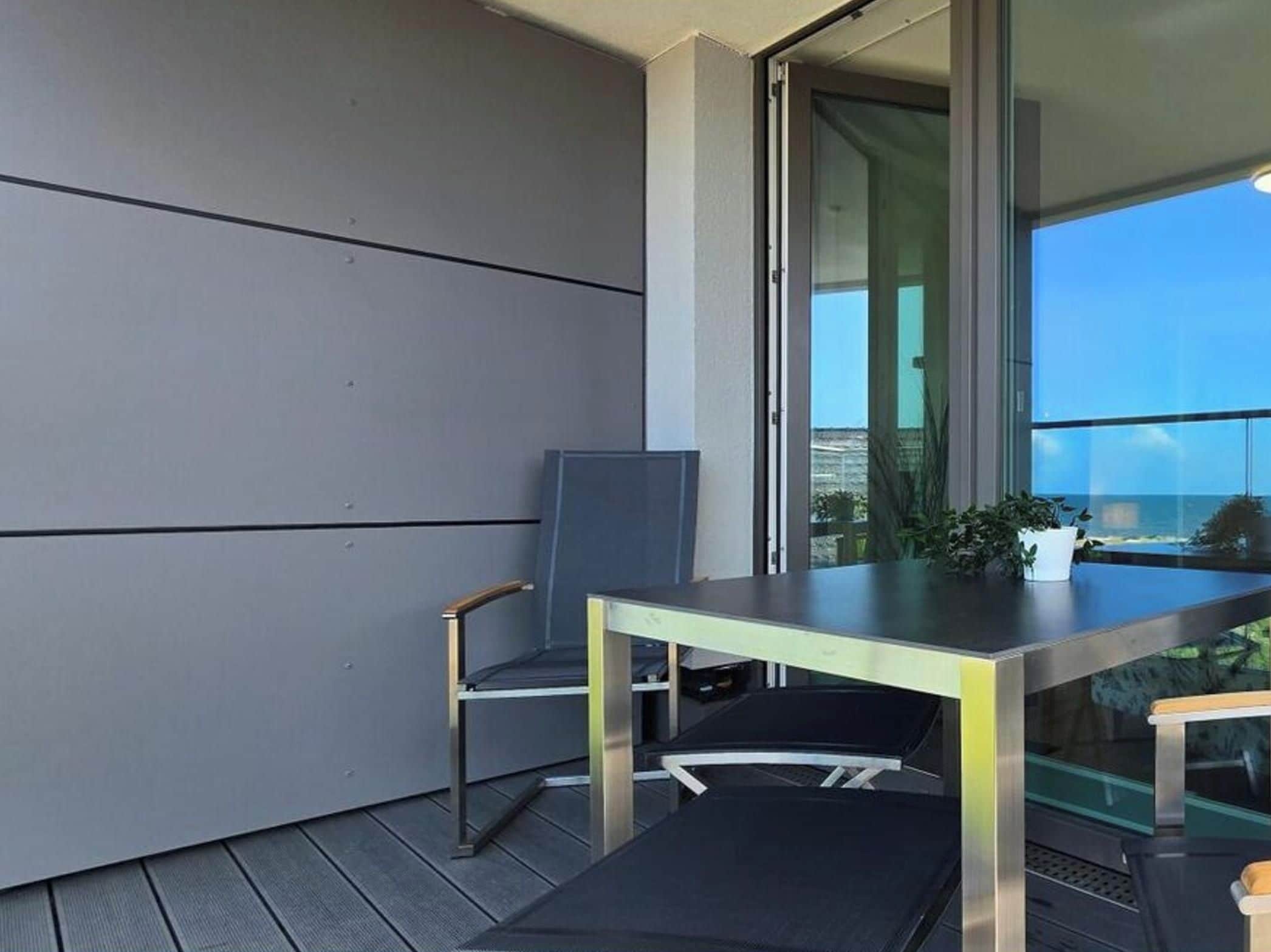 Uma varanda com mesa e cadeiras, um vaso de plantas e vista para o oceano.