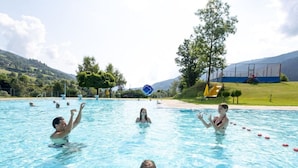 Piscina com várias pessoas na água, rodeada por um espaço gramado e árvores.
