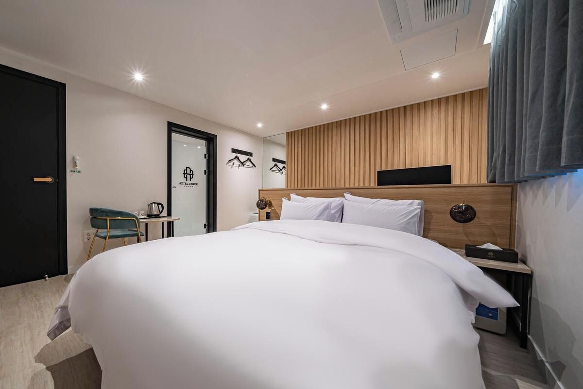 Quarto de hotel moderno com uma cama grande, cabeceira de madeira, mesa de cabeceira e uma cadeira.