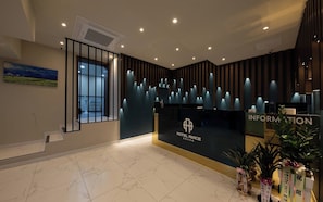Uma área de recepção de hotel com design moderno, apresentando um balcão de atendimento, um painel informativo fixado na parede e uma grande janela.