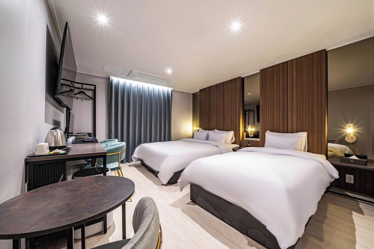 Quarto de hotel com duas camas, uma escrivaninha, uma cadeira e uma televisão.