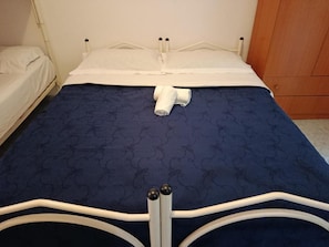 Uma cama com cabeceira e peseira brancas, um cobre-leito azul e uma toalha branca enrolada sobre a cama.