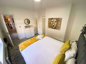 Quarto de hotel com cama, mesa de cabeceira, espelho, quadro e guarda-roupa.