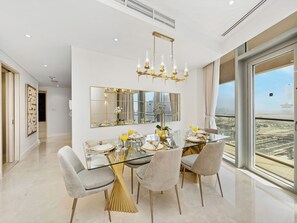 Espaço de refeições moderno com mesa de vidro, detalhes dourados e vista para a cidade.